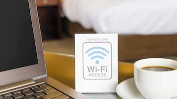 Um laptop, o símbolo de acesso Wi-Fi e uma xícara de café sobre uma mesa de hotel.
