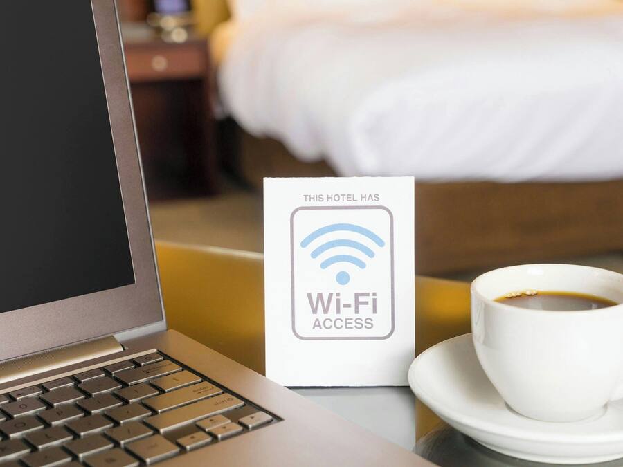 Um laptop, o símbolo de acesso Wi-Fi e uma xícara de café sobre uma mesa de hotel.