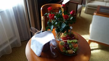 Uma mesa com um vaso de rosas vermelhas, uma taça de vinho e um prato de frutas.