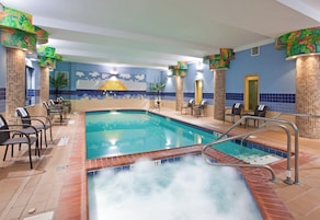 Piscina com hidromassagem, rodeada por cadeiras e uma parede revestida com mosaicos.
