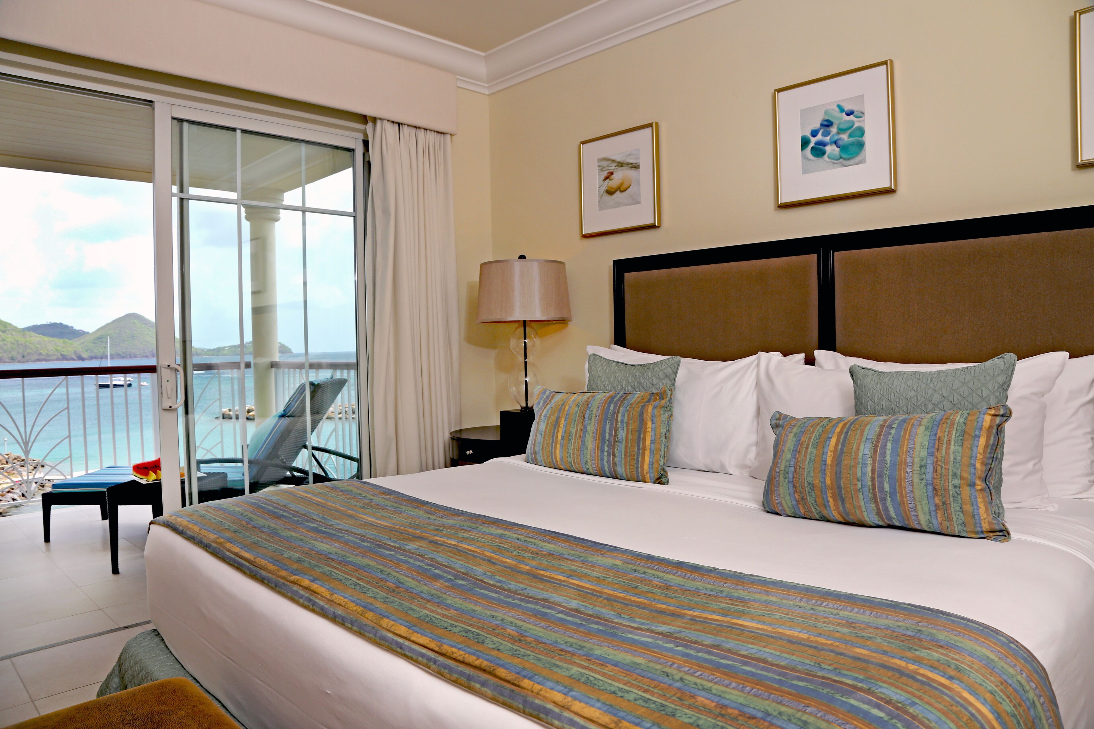 Quarto de hotel com uma cama grande, uma varanda com vista para o mar e duas molduras na parede.