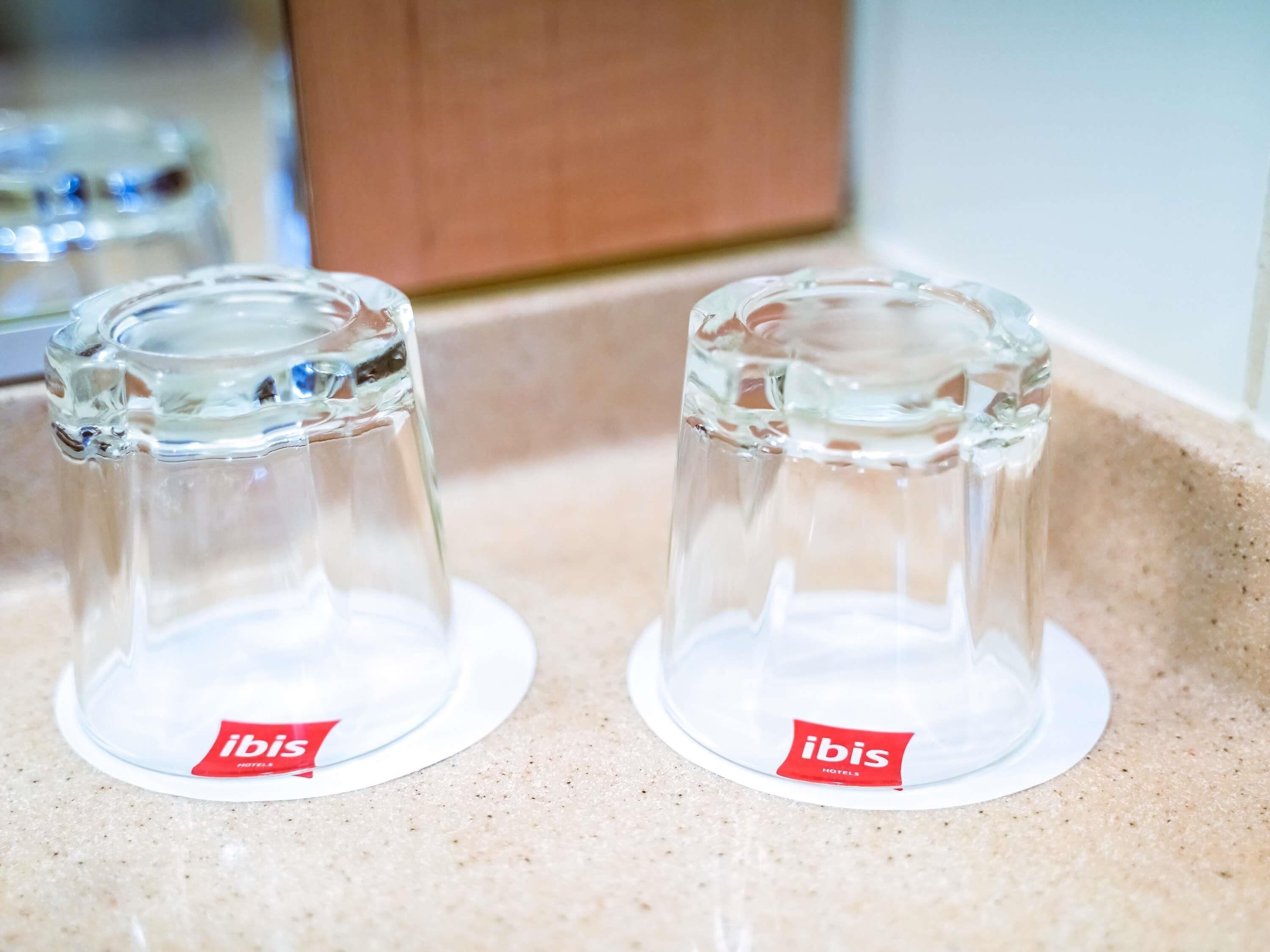Dois copos de vidro transparente com a etiqueta 'ibis hotels' em uma bancada.