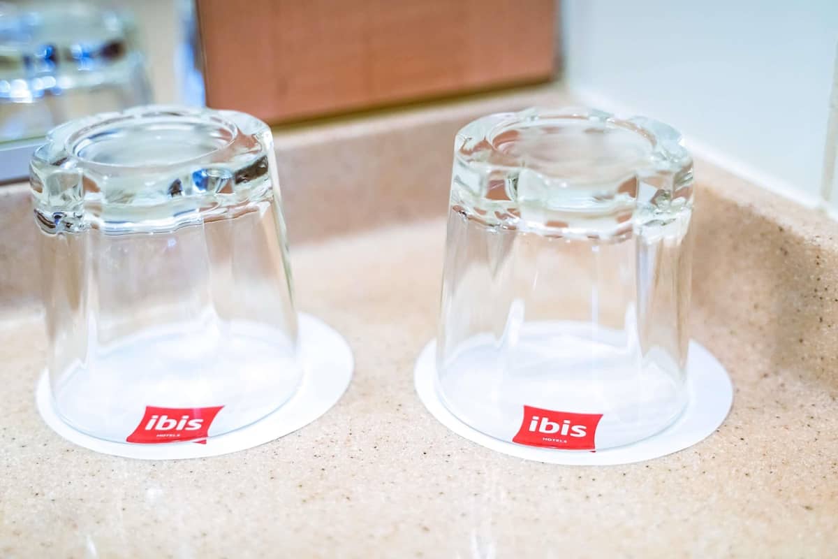 Dois copos de vidro transparente com a etiqueta 'ibis hotels' em uma bancada.