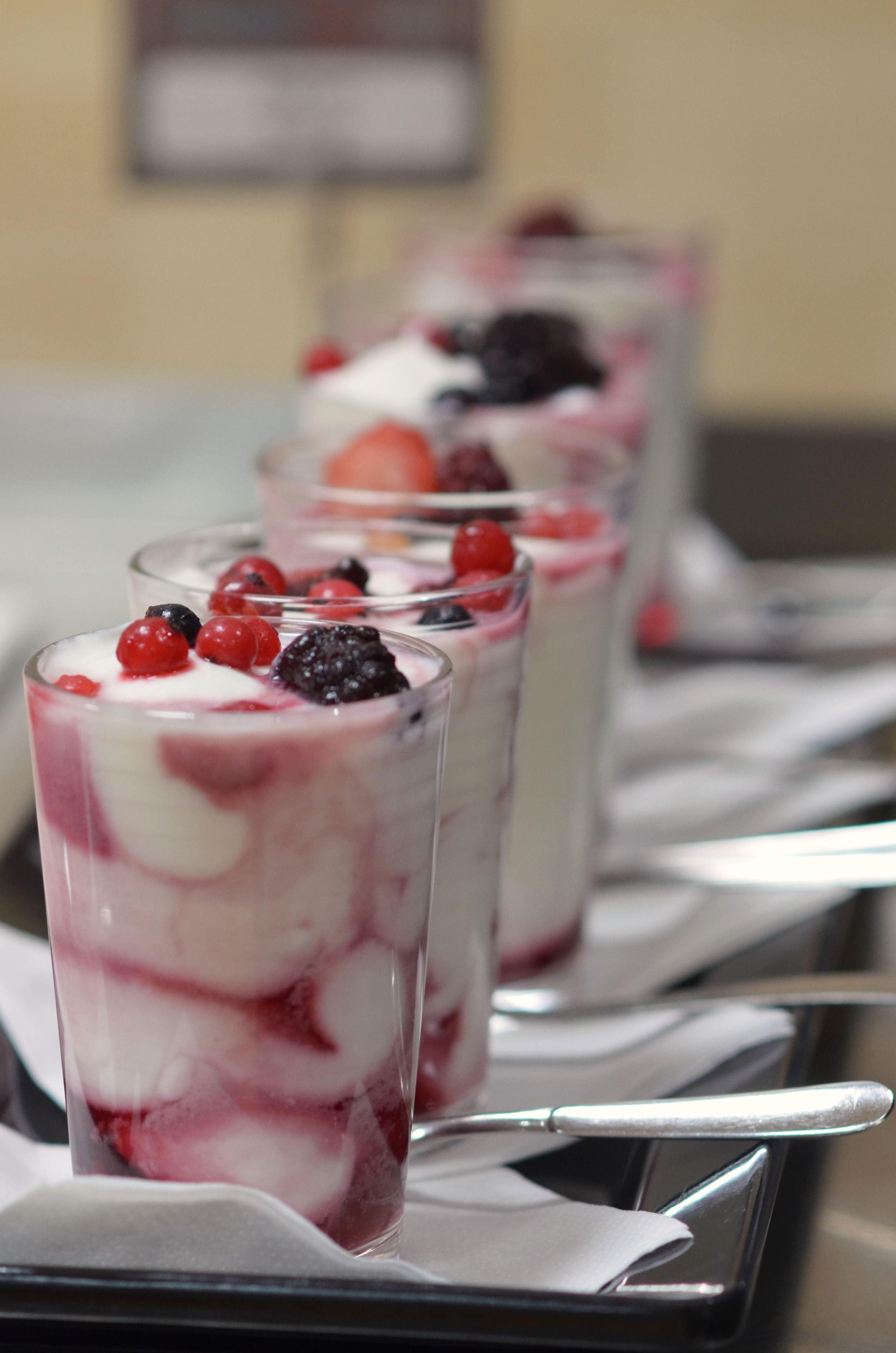 Uma fileira de copos transparentes com sobremesas em camadas, cada um coberto com frutos vermelhos.