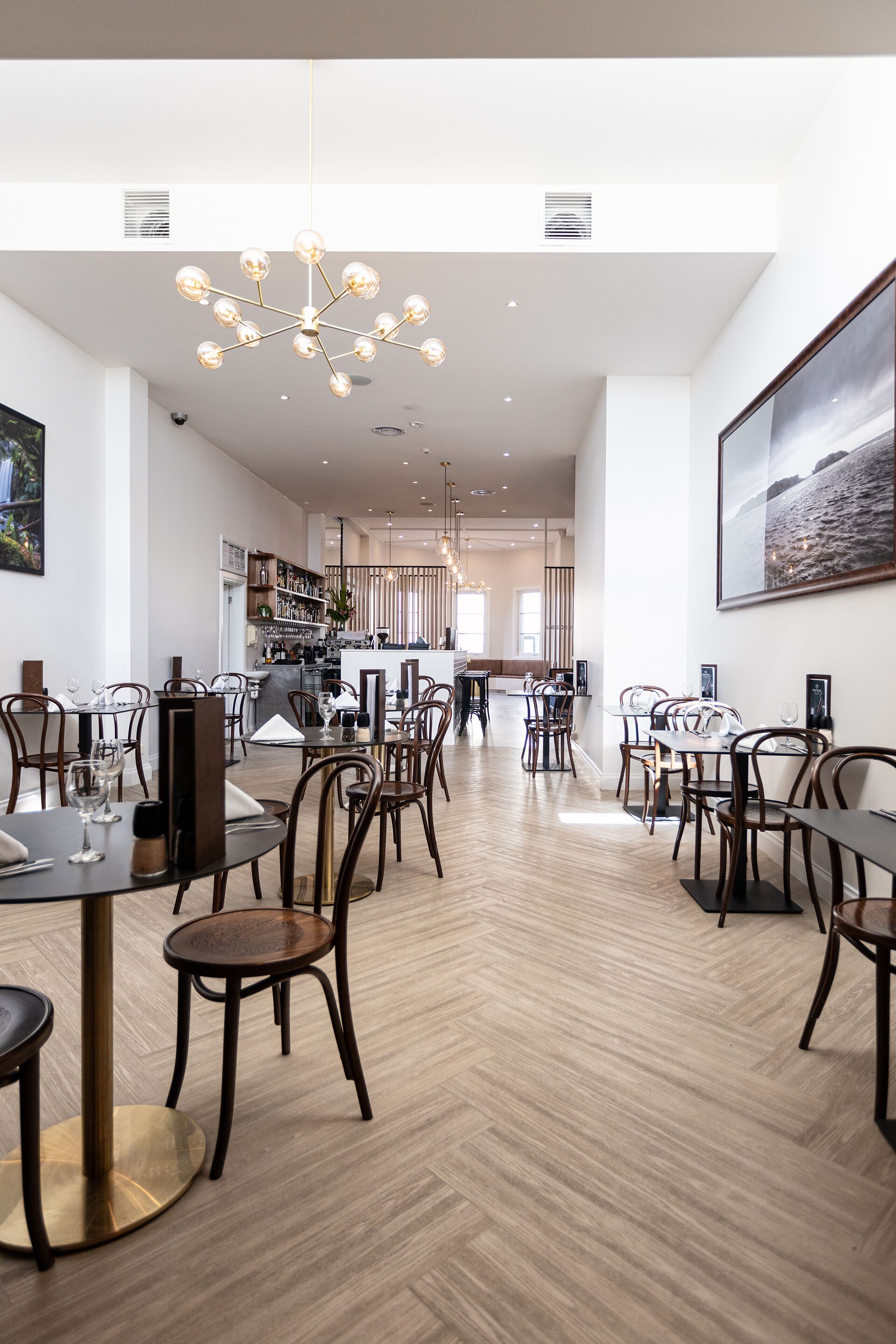 Um restaurante amplo com piso de madeira, mesas redondas e lustres modernos.