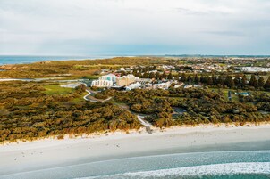 Vista aérea de uma estância costeira com um edifício grande, frente mar e vegetação ao redor.