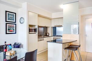 Uma cozinha moderna com armários brancos, micro-ondas, fogão e uma mesa de jantar de vidro com cadeiras.