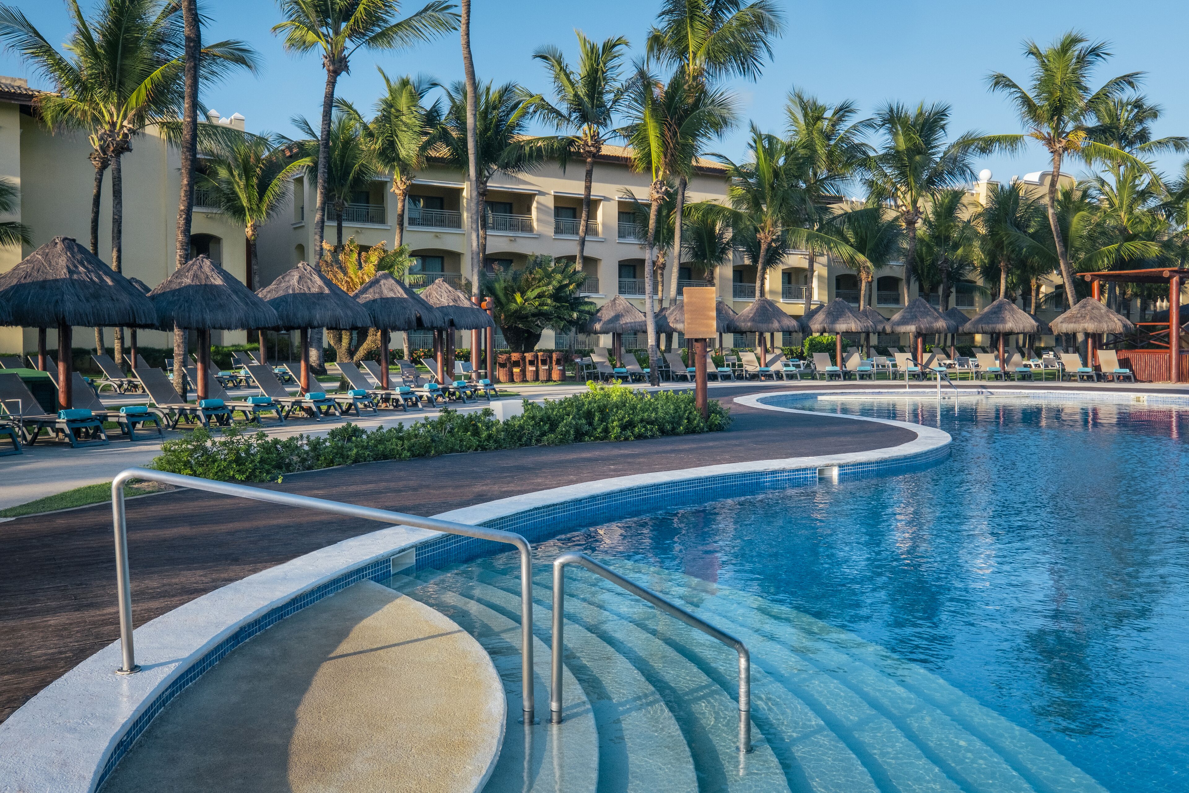 Área de piscina do resort com espreguiçadeiras e palmeiras.
