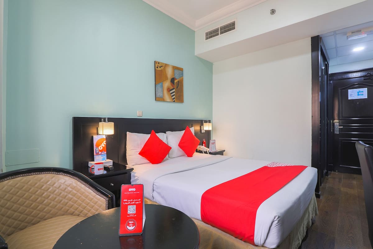 Quarto de hotel com cama, mesa de cabeceira, cadeira, mesa e uma obra de arte na parede.