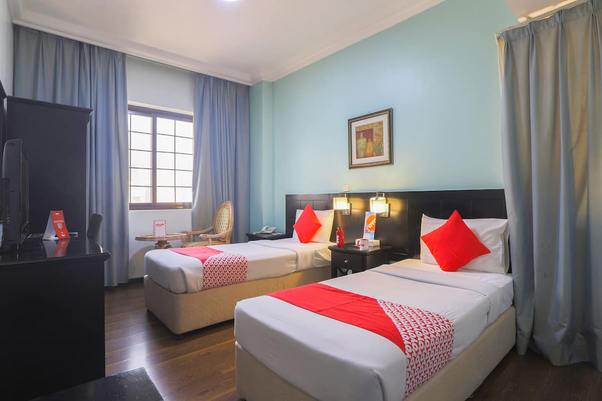 Quarto de hotel com duas camas, uma escrivaninha, uma cadeira e uma televisão.