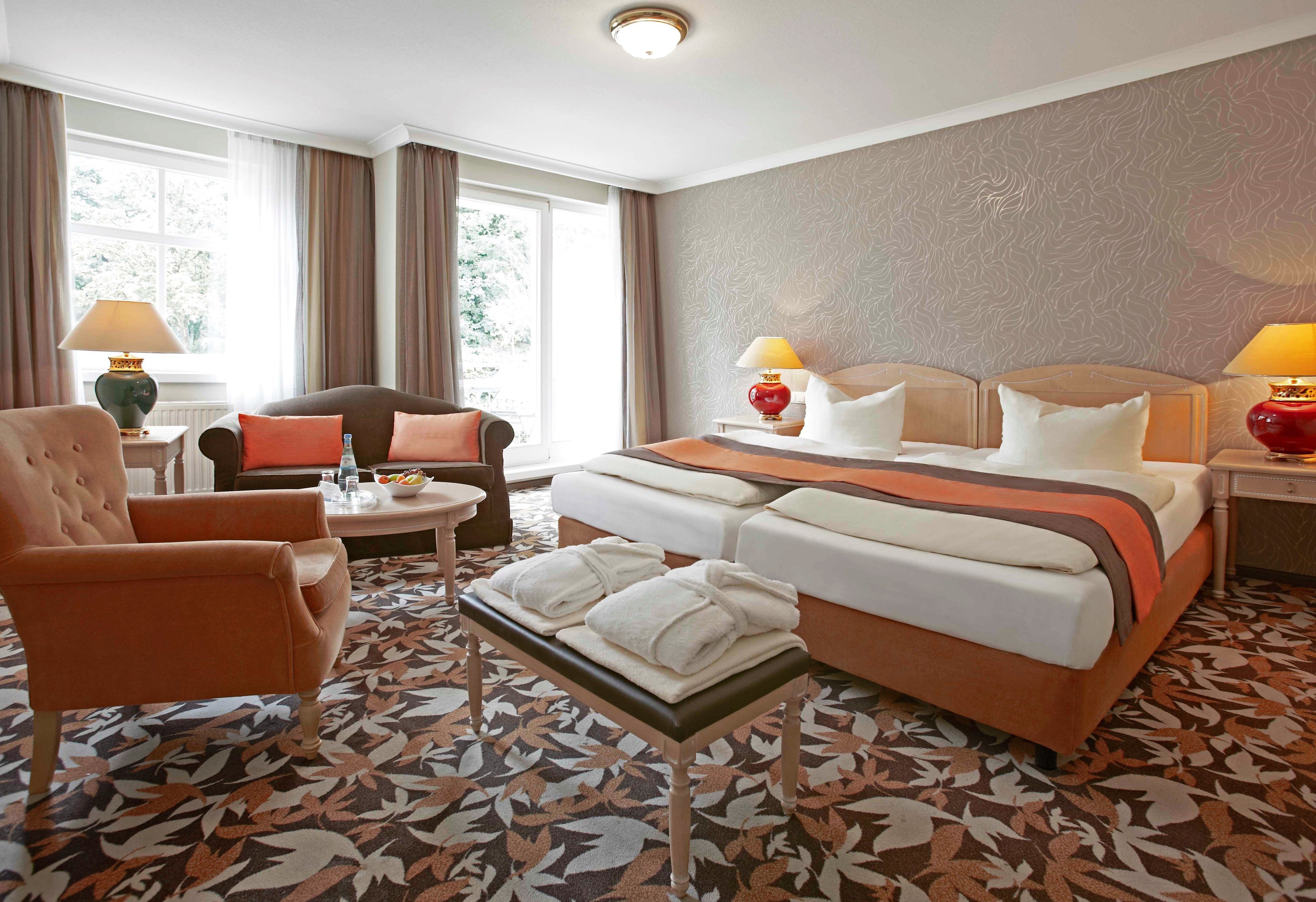 Quarto de hotel com cama, duas poltronas, uma mesinha e um sofá.