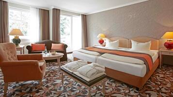 Quarto de hotel com cama, duas poltronas, uma mesinha e um sofá.