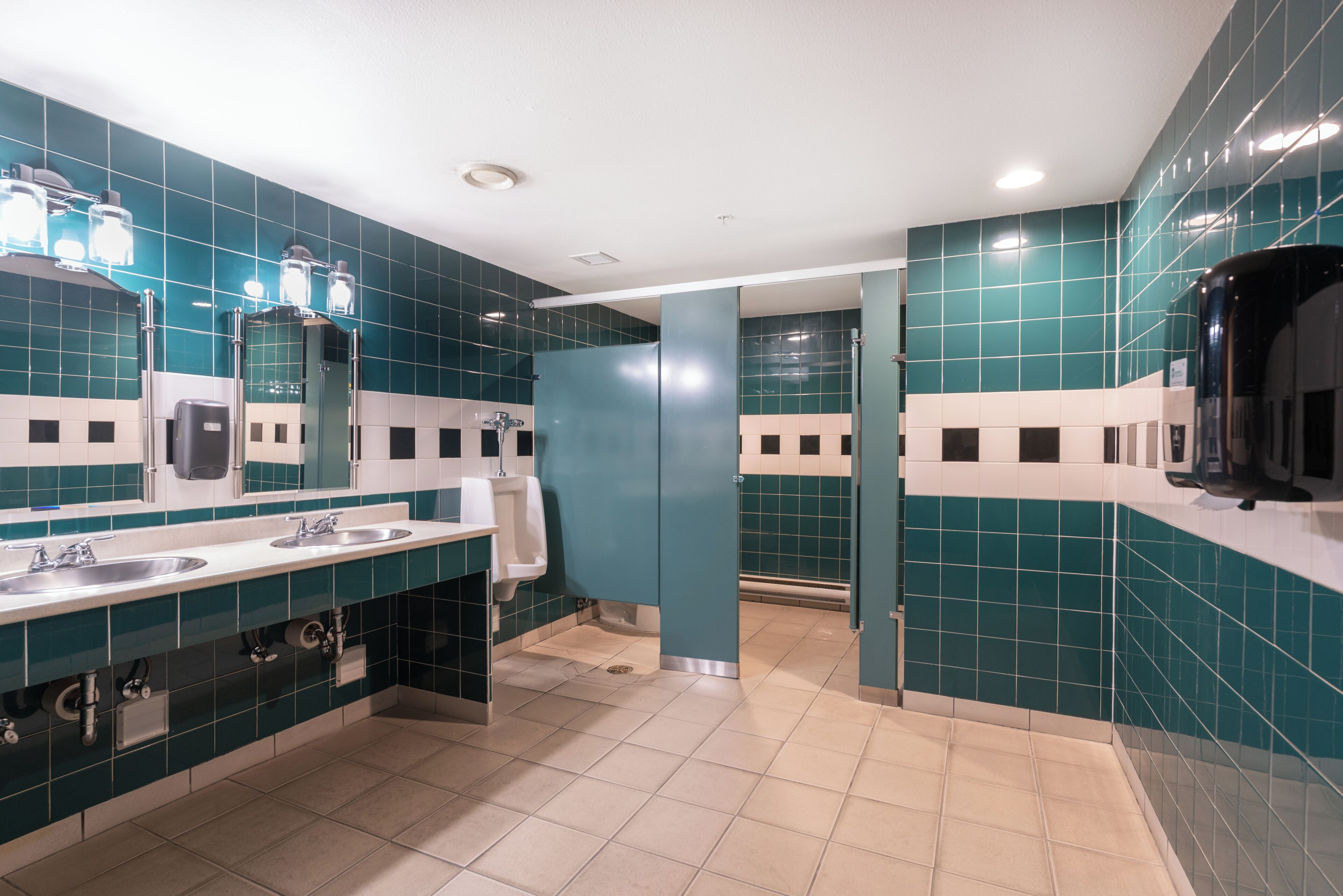 Um banheiro moderno com azulejos verde-água, duas pias, um espelho e área de chuveiro.