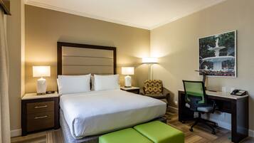 Quarto de hotel com uma cama grande, duas mesas de cabeceira com abajures, uma escrivaninha com cadeira e um quadro na parede.