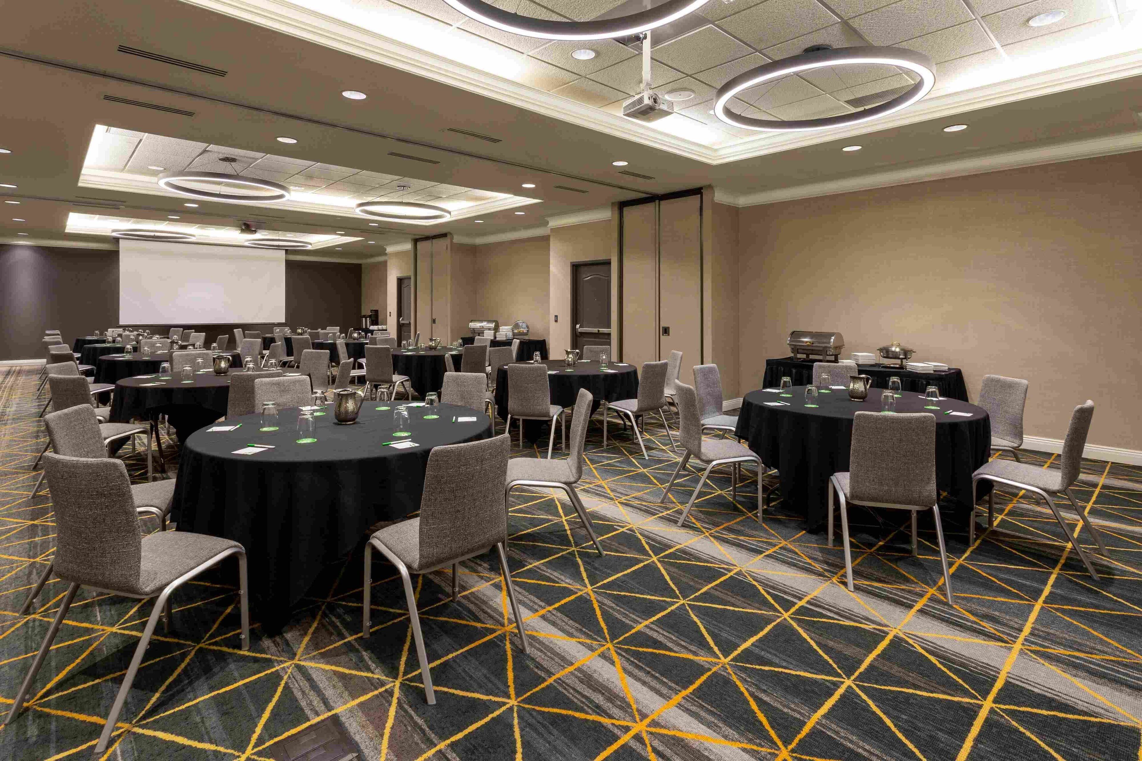 Uma sala de conferências com várias mesas redondas, cadeiras e uma tela grande.