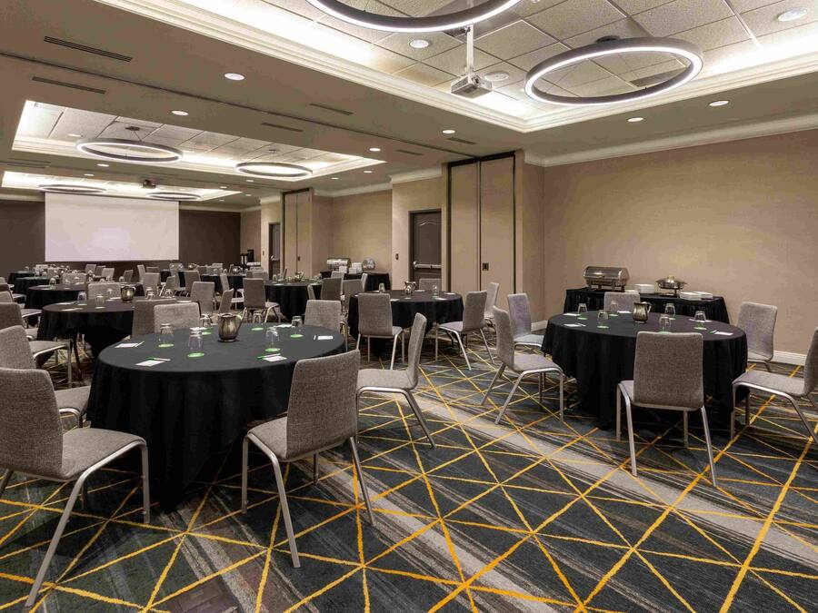 Uma sala de conferências com várias mesas redondas, cadeiras e uma tela grande.