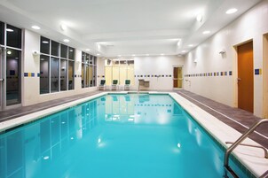 Piscina com água azul cristalina, rodeada por paredes brancas e chão revestido com azulejos.