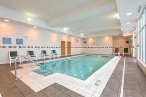 Piscina interna com piso ladrilhado, escada para piscina e várias cadeiras ao longo da parede.