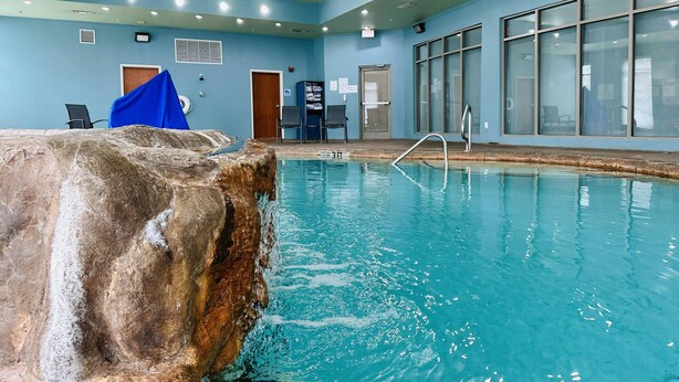 Piscina interior com borda rochosa, parede azul e teto com iluminação embutida.
