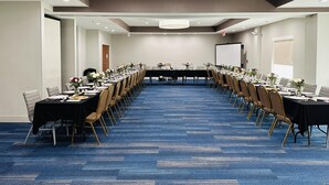 Uma sala de conferências com mesas compridas, cadeiras e uma tela de projeção.