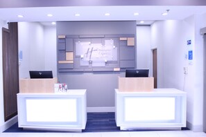 Uma área de recepção com dois balcões, um painel de exibição digital e um tapete azul.