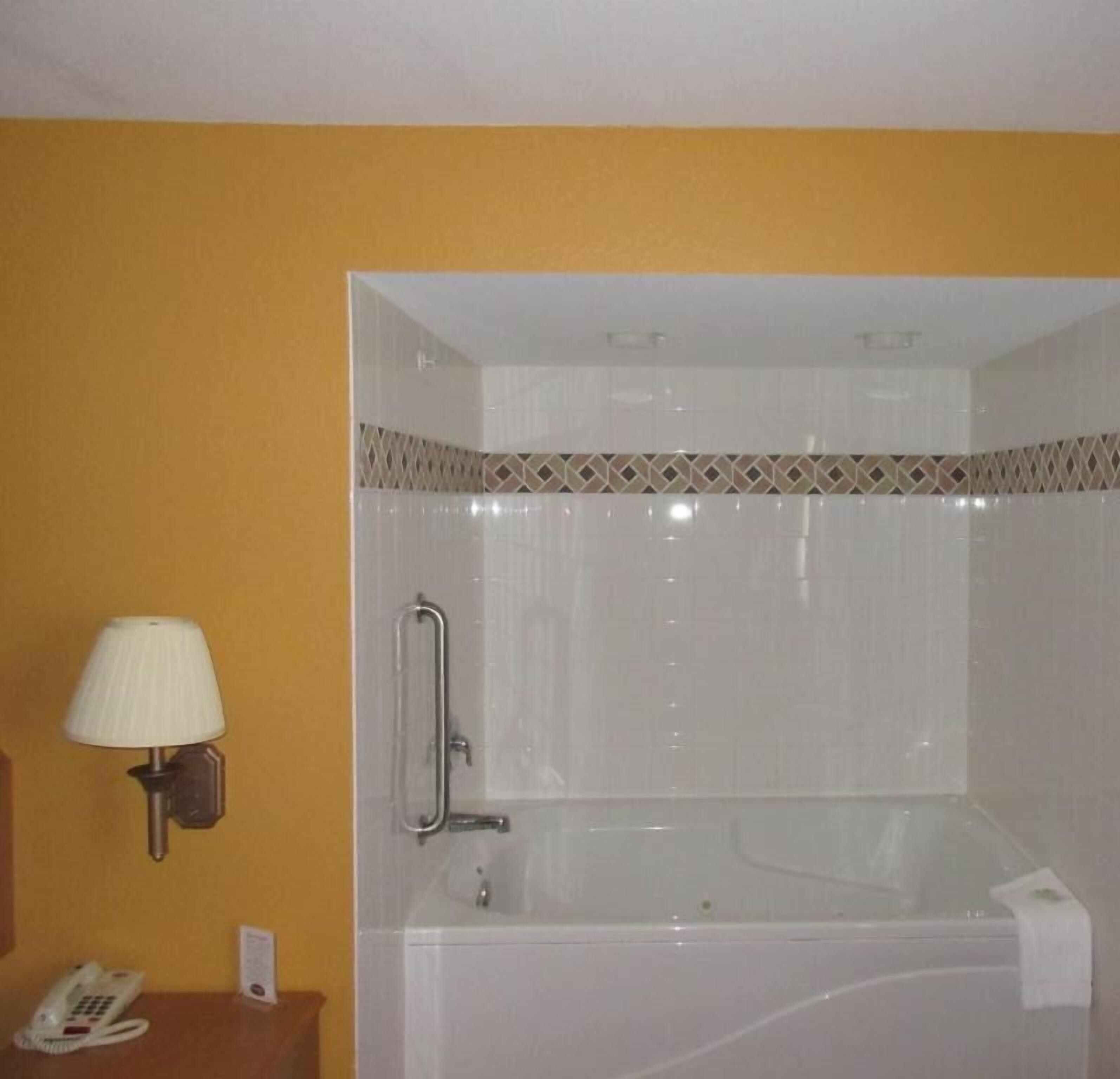 Uma casa de banho com uma banheira branca, um suporte de papel higiénico na parede e um telefone num criado-mudo.