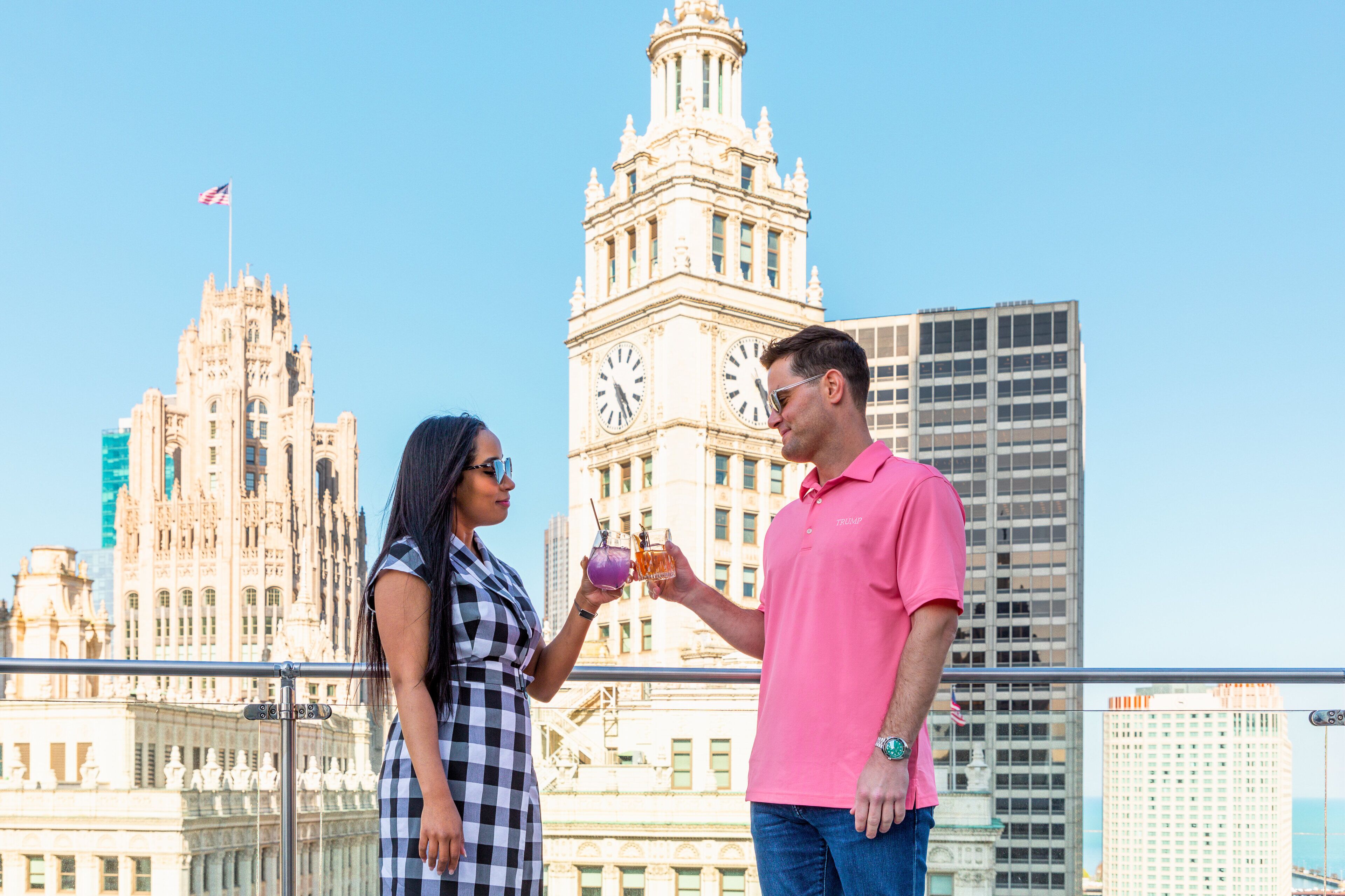 Um casal segurando bebidas com um edifício histórico e torre do relógio ao fundo.