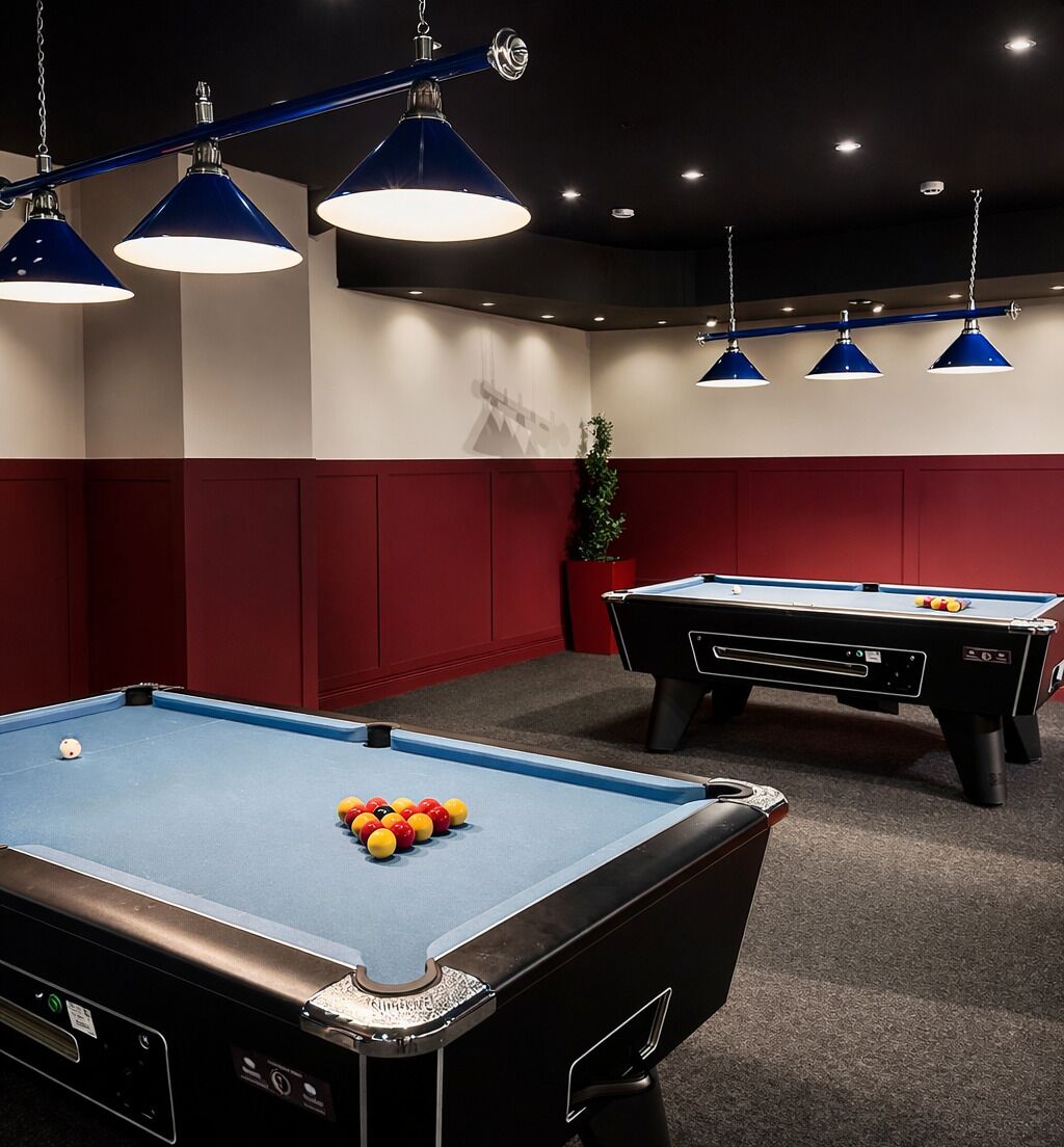 Uma mesa de bilhar com bolas, outra mesa ao fundo e três luminárias pendentes.