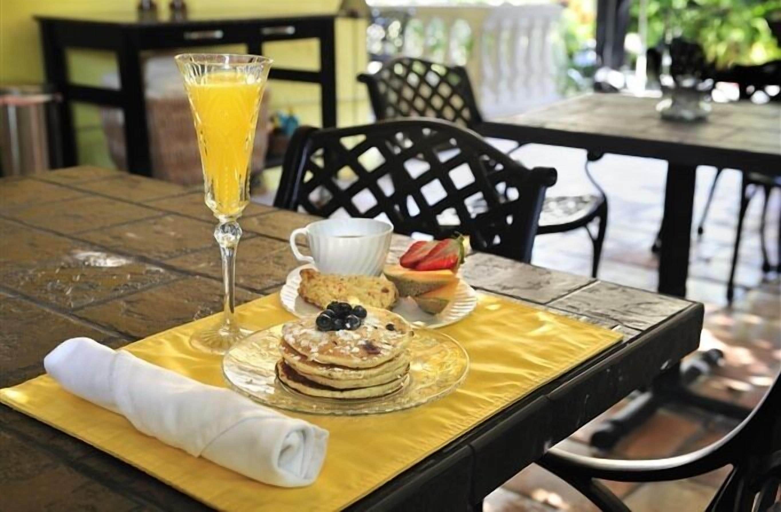 Mesa com panquecas, um copo de sumo de laranja e uma chávena de café sobre um guardanapo amarelo.
