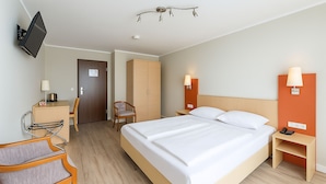 Quarto de hotel com cama, mesas de cabeceira, escrivaninha com cadeira, televisão na parede e porta que dá para outro quarto.
