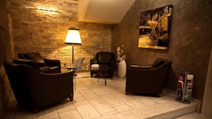 Um hall com paredes de pedra, poltronas de couro, uma mesa com abajur e um quadro.