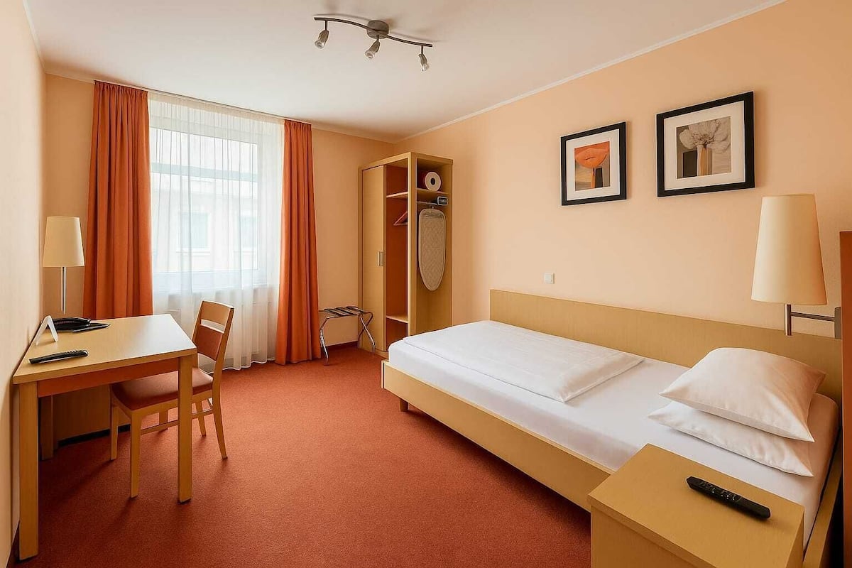Quarto de hotel com cama, escrivaninha, cadeira, guarda-roupa e duas molduras na parede.