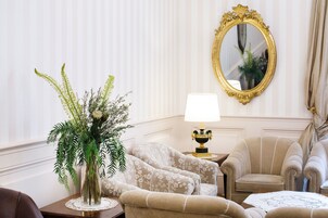 Um quarto com um arranjo floral, duas poltronas, uma luminária e um espelho na parede.