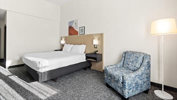 Quarto de hotel com cama, uma cadeira, luminária e mesa de cabeceira com telefone.