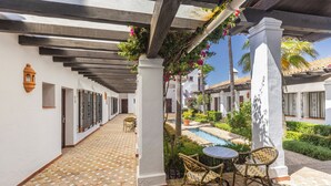 Uma galeria coberta com piso de azulejos, pilares brancos e assentos externos.