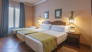 Quarto de hotel com duas camas, uma mesa de cabeceira, uma luminária e uma janela com cortinas.