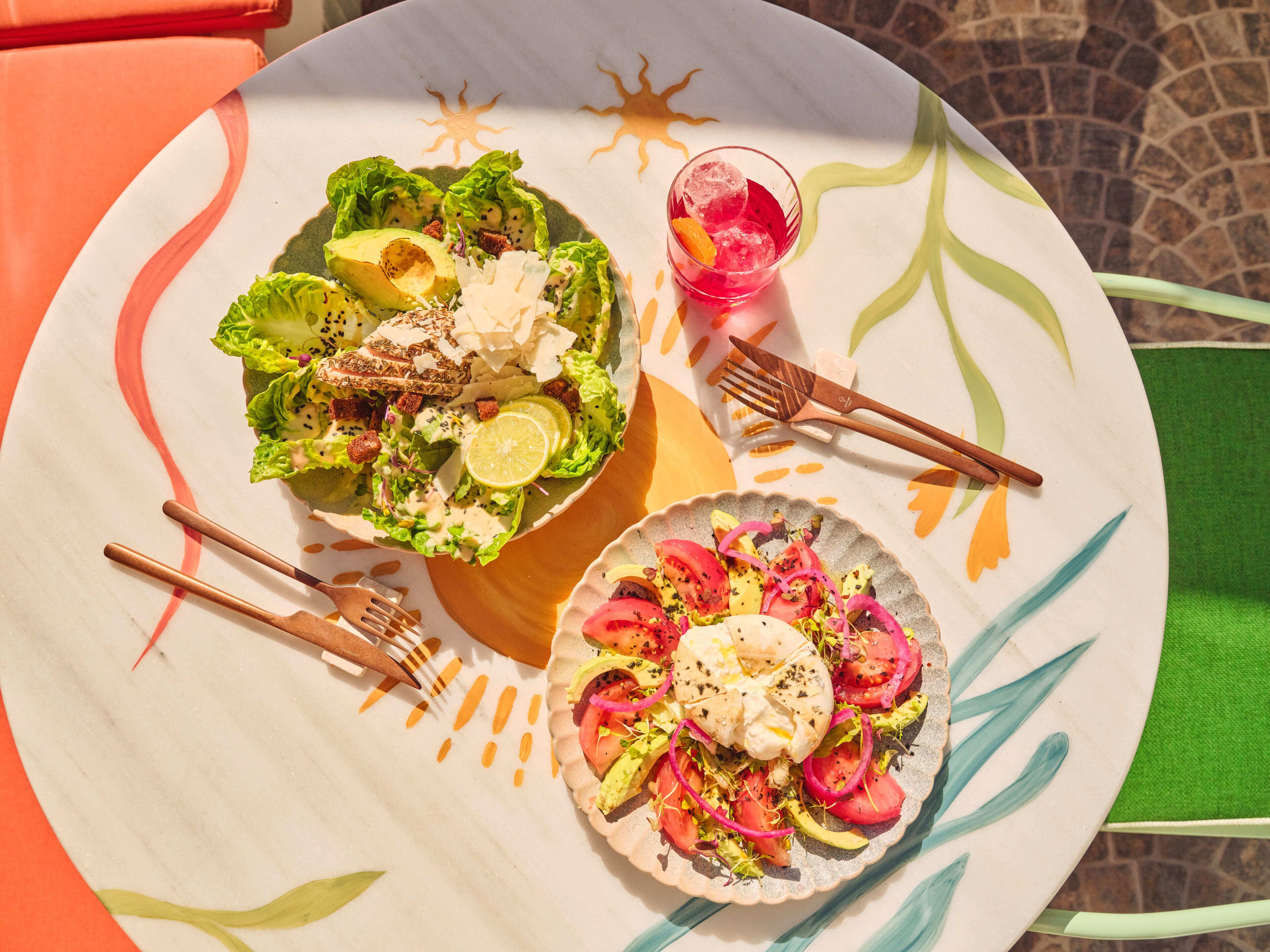 Uma mesa com duas saladas, uma bebida e talheres.