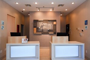 Uma área de recepção com design moderno, incluindo um balcão de atendimento, uma placa na parede e teto com iluminação embutida.