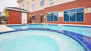 Piscina com borda em azulejo, prédio de tijolos com janelas e placa indicando ausência de salva-vidas.