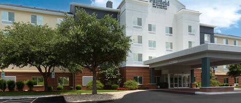 Um hotel Fairfield Inn & Suites com entrada coberta, estacionamento e vegetação ao redor.