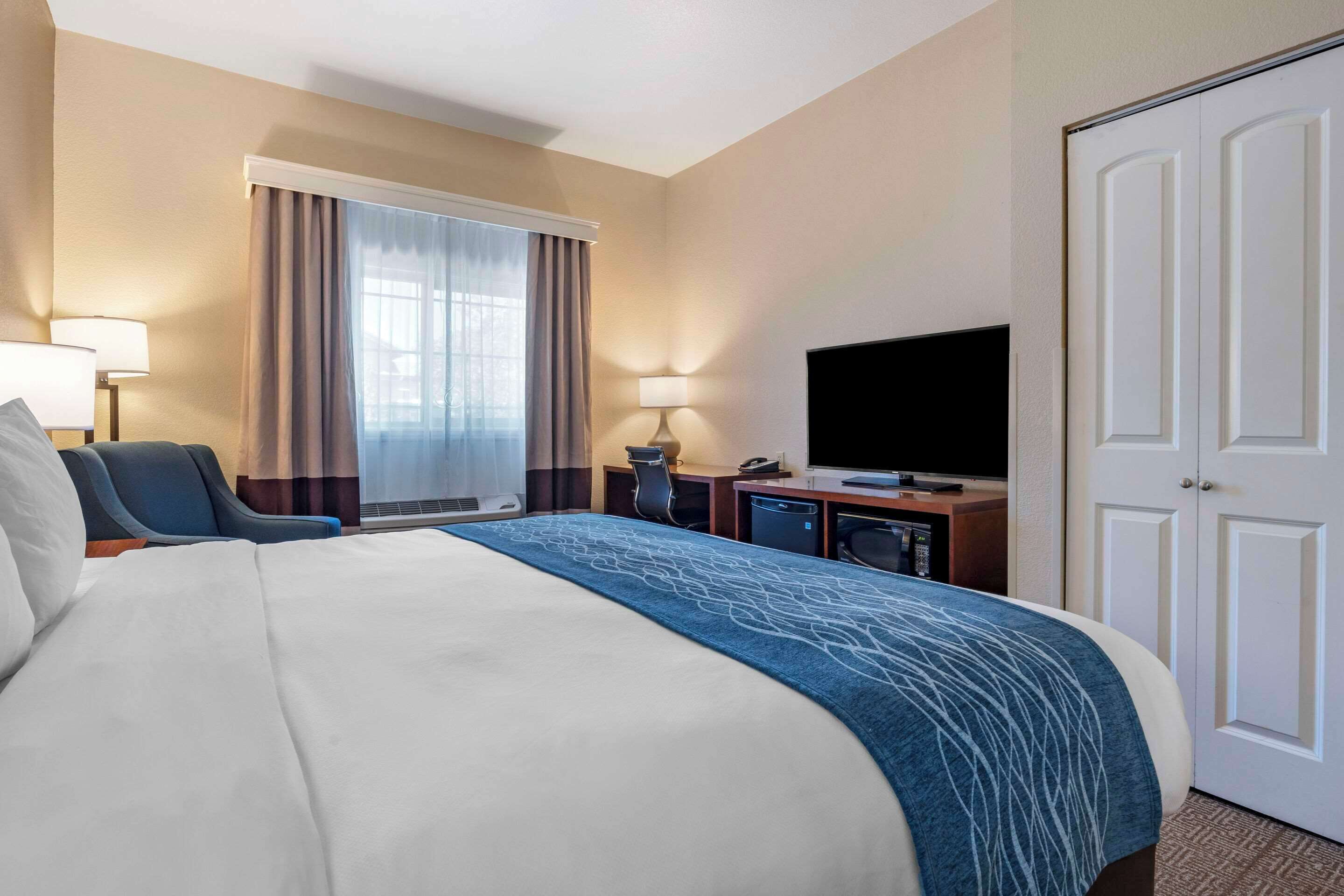 Quarto de hotel com uma cama grande, uma escrivaninha com um computador, uma televisão e um guarda-roupa.