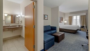 Quarto de hotel com banheiro, uma cama, um sofá e uma escrivaninha.