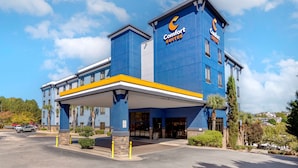 Um hotel Comfort Suites com fachada azul e amarela, entrada coberta e estacionamento.