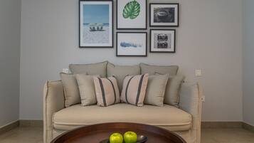 Uma sala de estar com um sofá bege, uma mesa de centro com duas maçãs verdes e quatro quadros na parede.