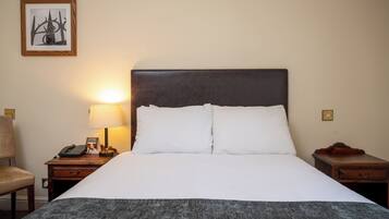 Quarto de hotel com uma cama grande, abajur, telefone, quadro na parede e mesa de cabeceira de madeira.