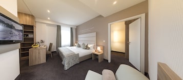 Quarto de hotel com cama, mesa de cabeceira, abajur, televisão, escrivaninha, cadeira e guarda-roupa.