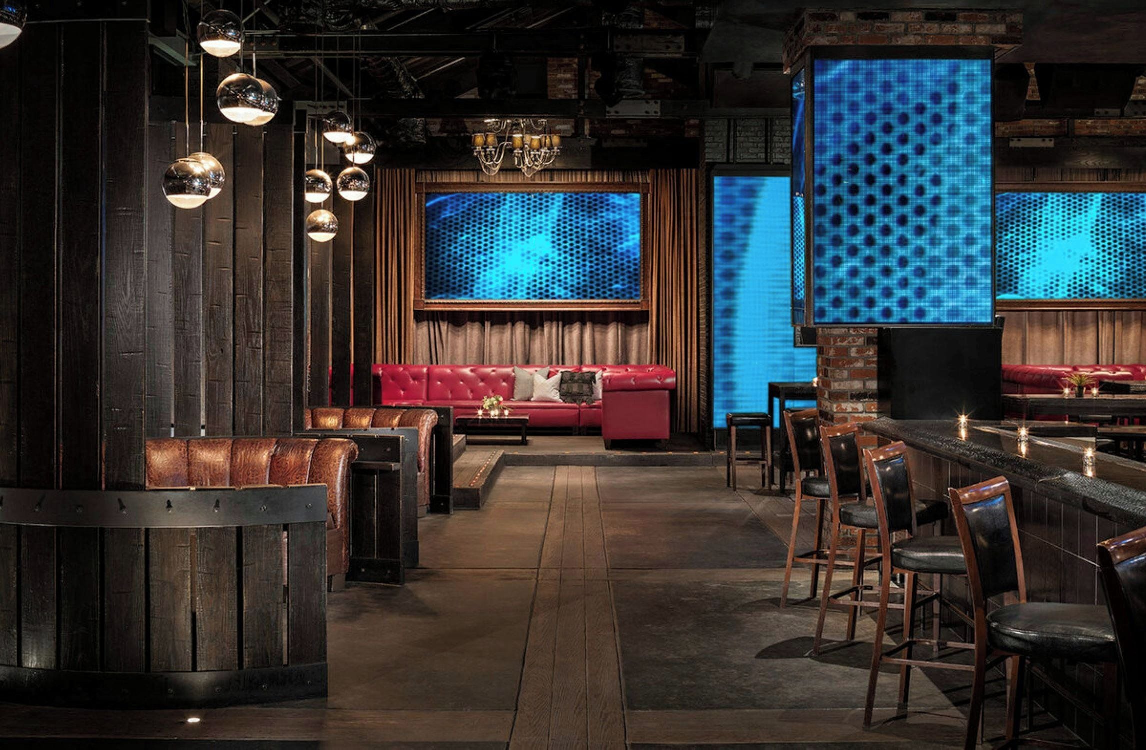 Uma área de bar com piso de madeira, assentos vermelhos e luminárias esféricas penduradas.