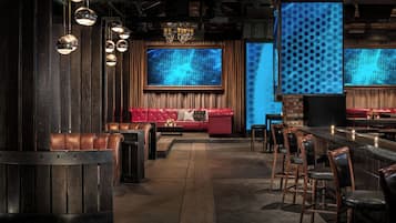 Uma área de bar com piso de madeira, assentos vermelhos e luminárias esféricas penduradas.
