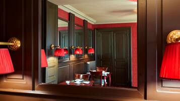 Quarto com um espelho refletindo uma área de refeições, incluindo uma mesa posta com pratos, copos e um abajur vermelho.