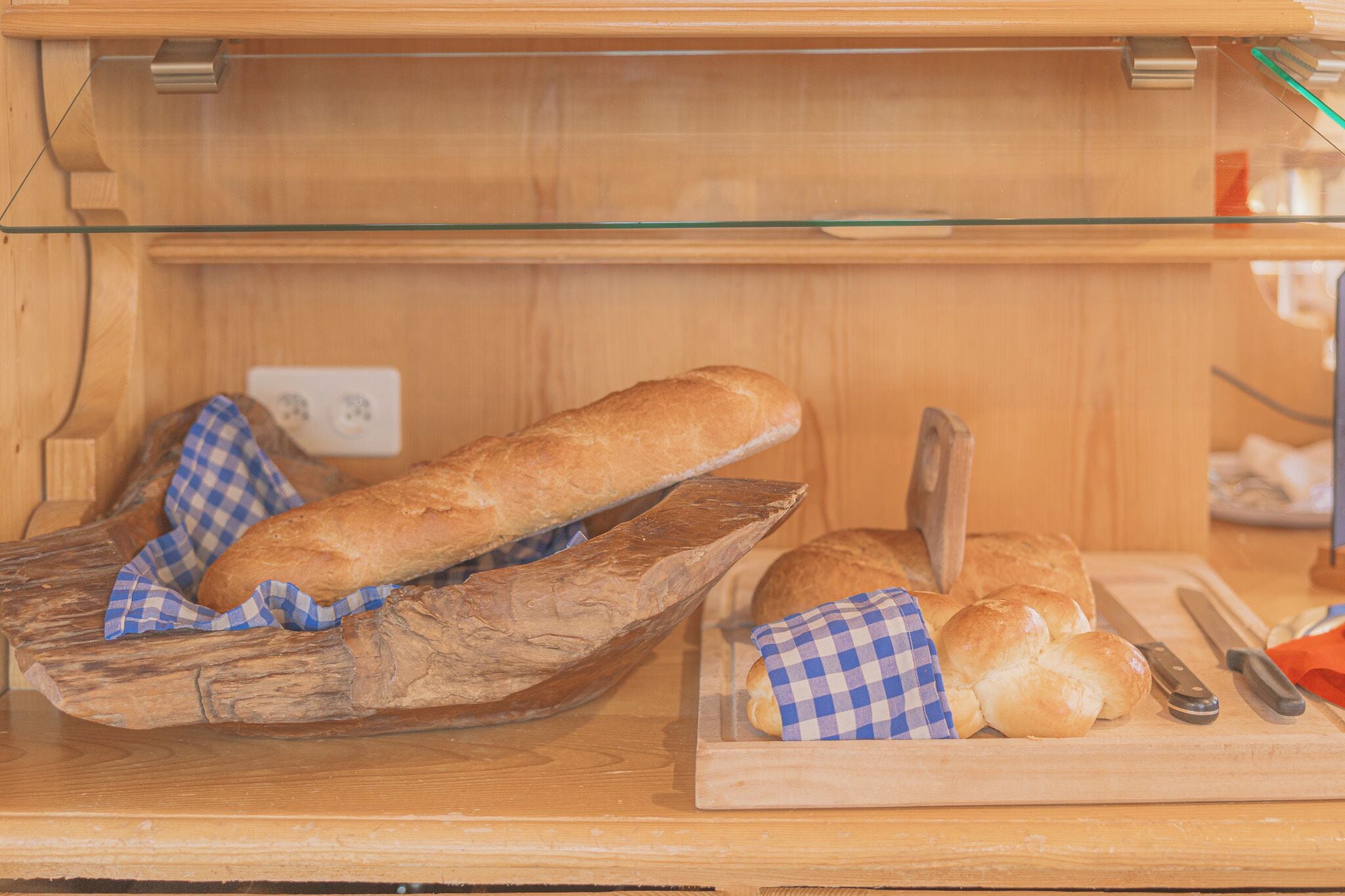 Uma mesa de madeira com pão, incluindo uma baguete e pães, uma tábua de corte e uma faca.
